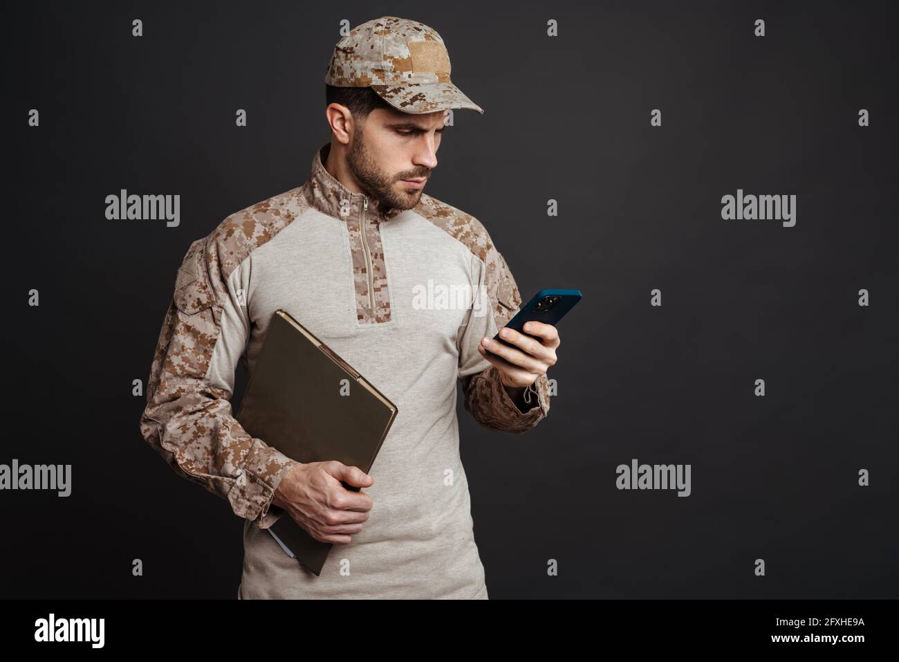 Serious military man using cellphone while posing with folder isolated ...
