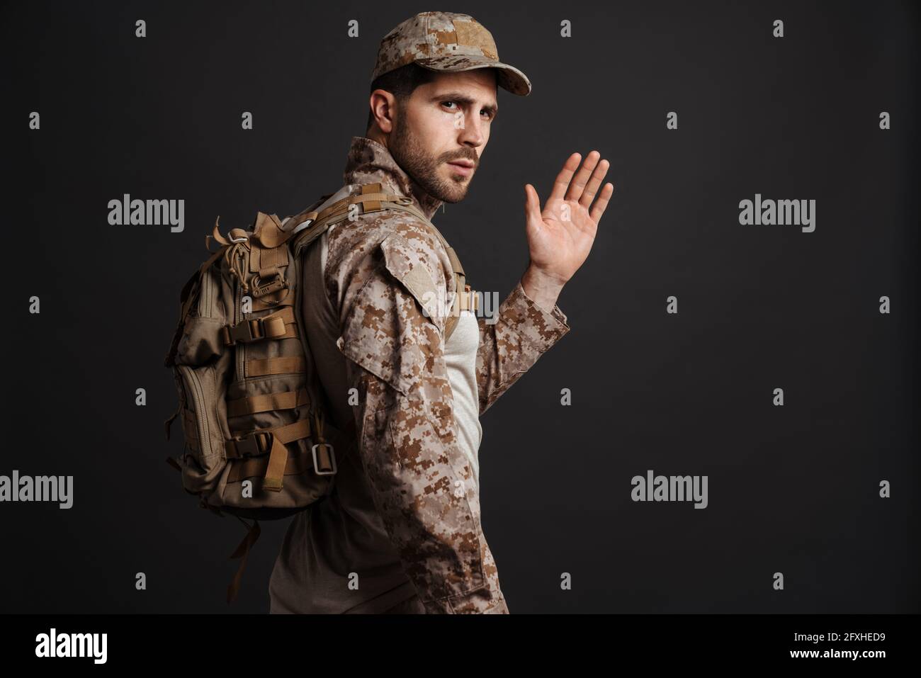 Confident masculine military man waving hand while posing with backpack ...