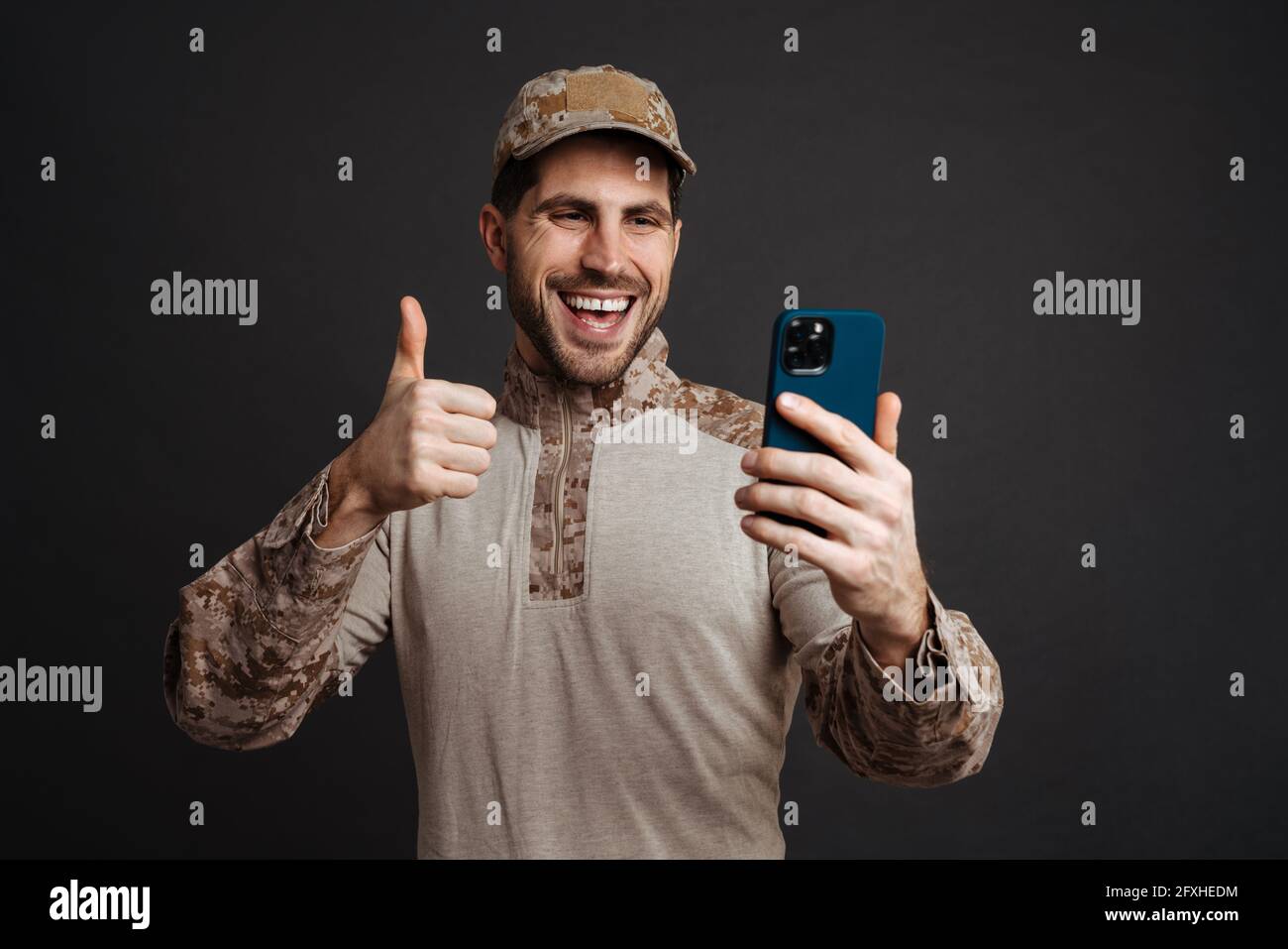 Happy military man showing thumb up and using mobile phone isolated ...