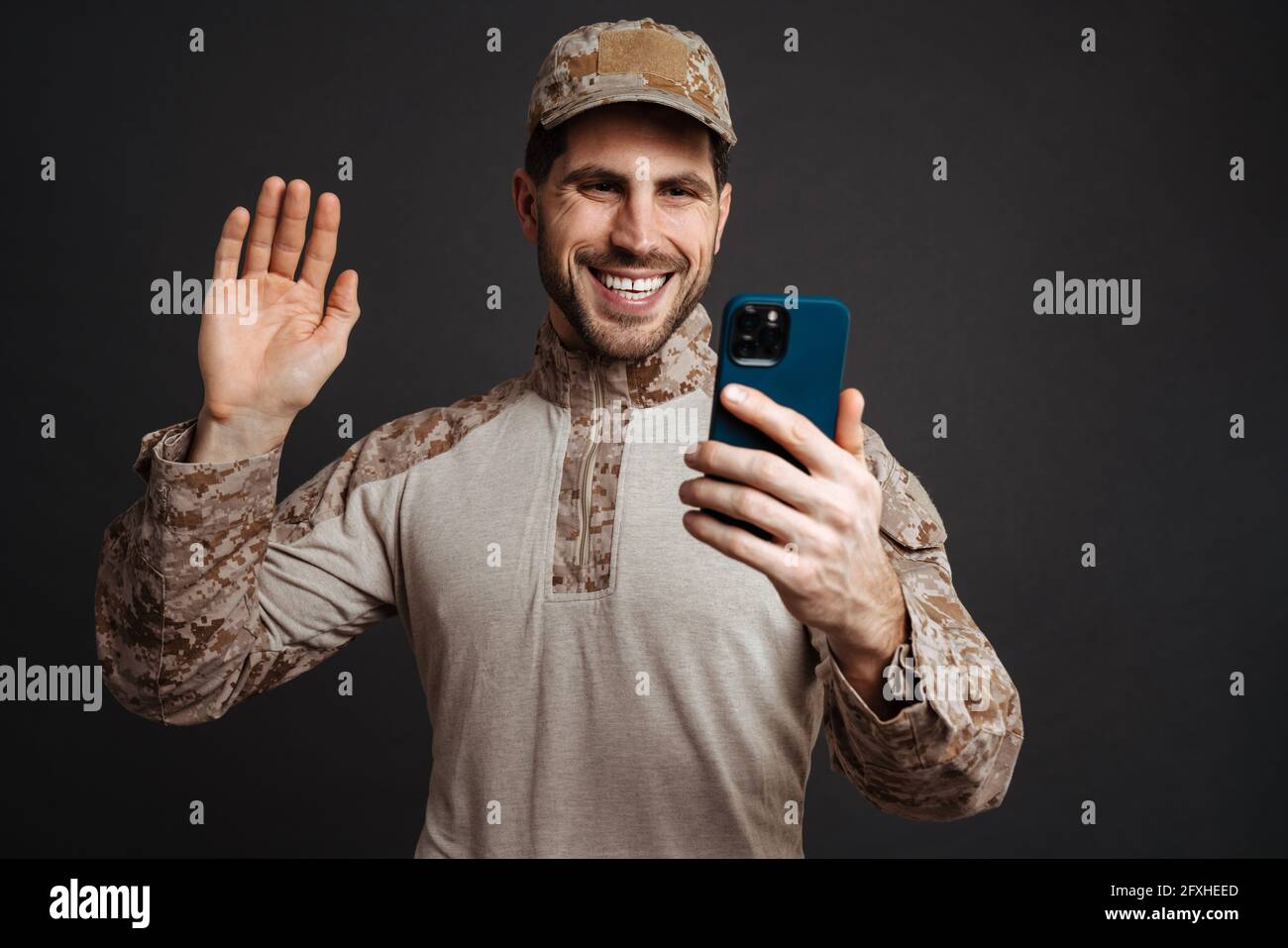 Happy military man waving hand and using mobile phone isolated over ...