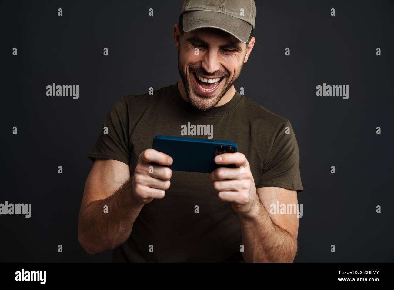 Happy masculine military man playing online game on mobile phone ...