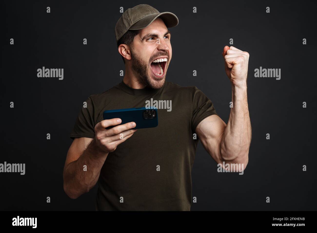 Excited masculine military man playing online game on mobile phone ...