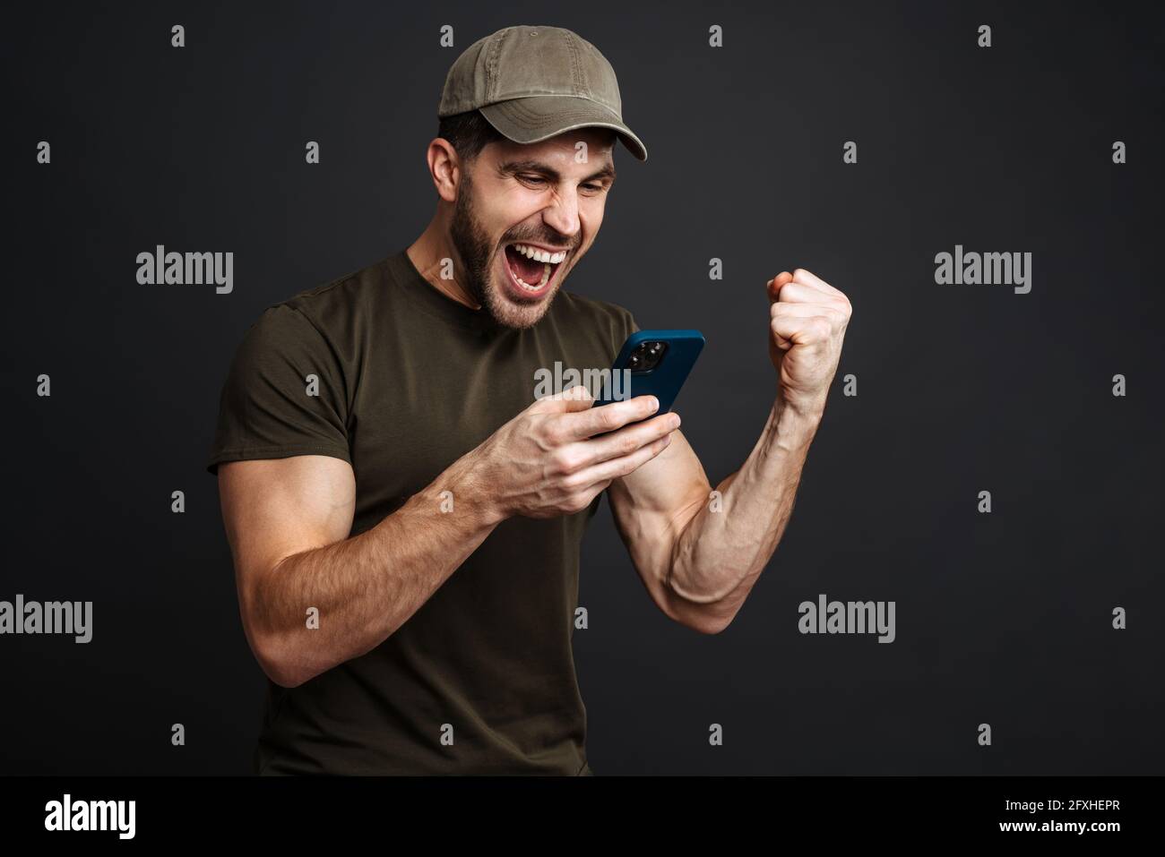 Excited military man making winner gesture while using cellphone ...