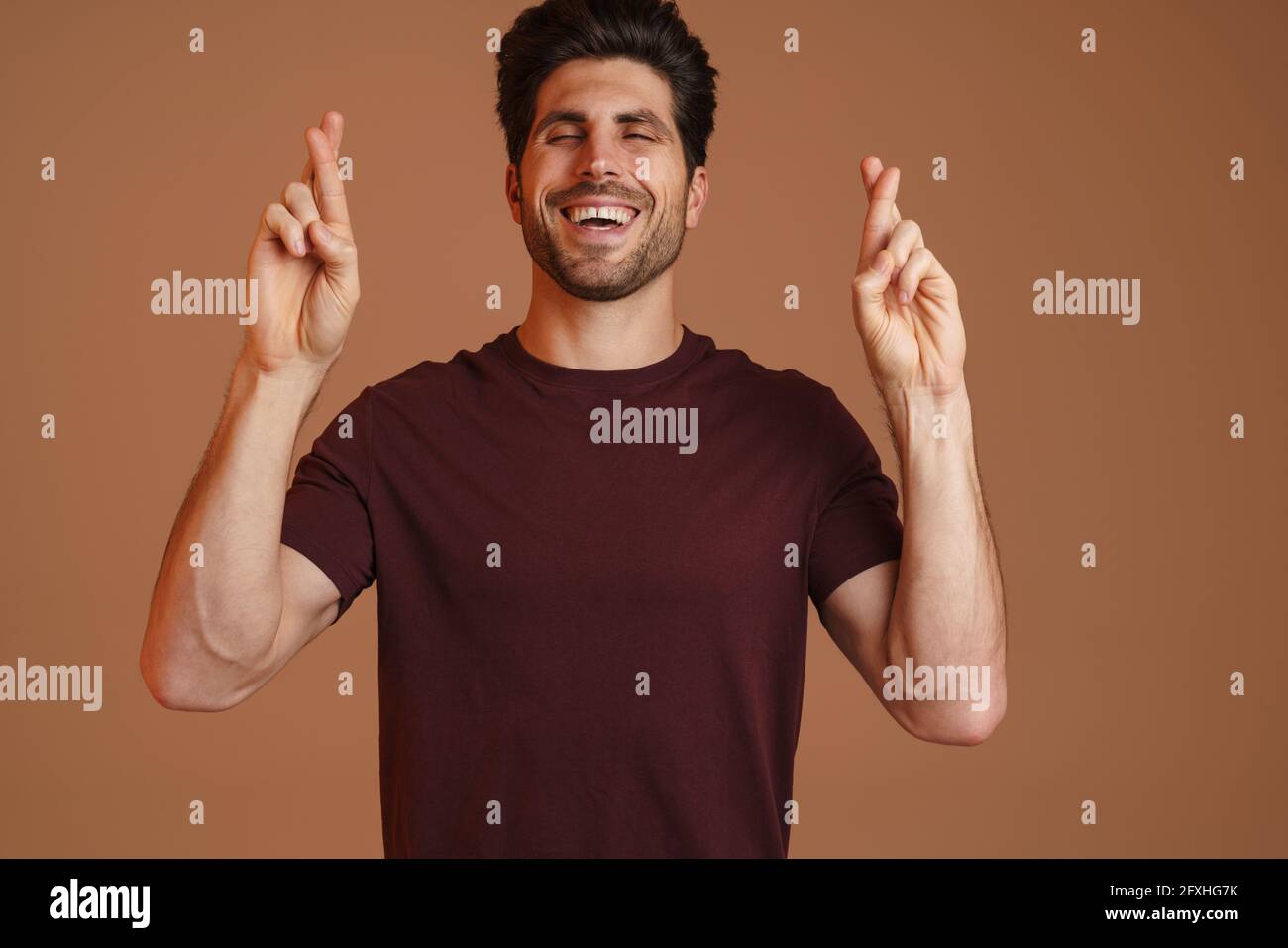 Joyful masculine man posing with fingers crossed for good luck isolated ...