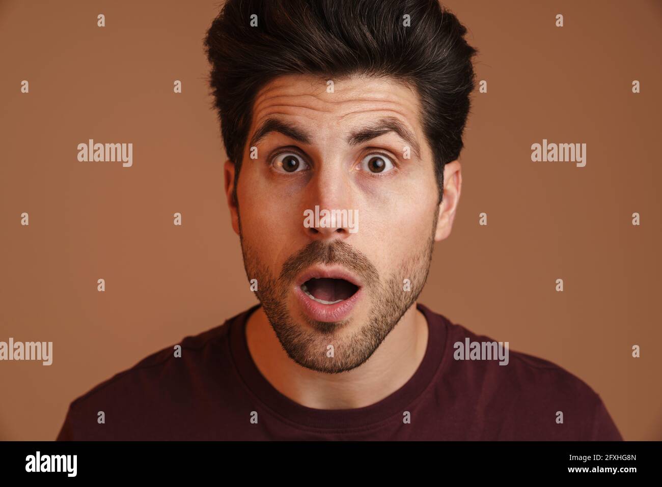 Shocked unshaven young man expressing surprise on camera isolated over ...