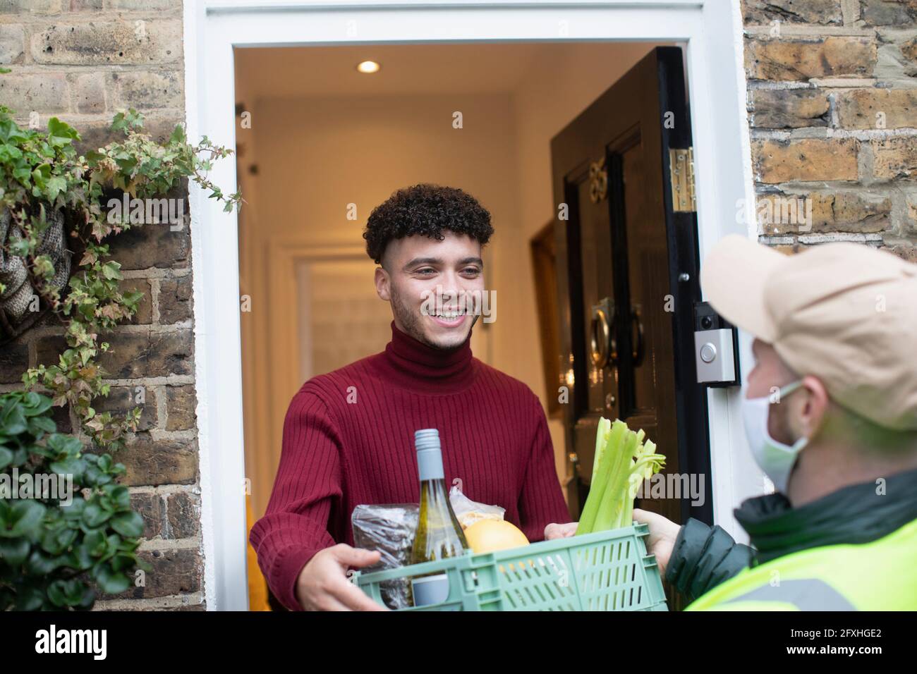 Happy man receiving grocery delivery from delivery man in face mask ...
