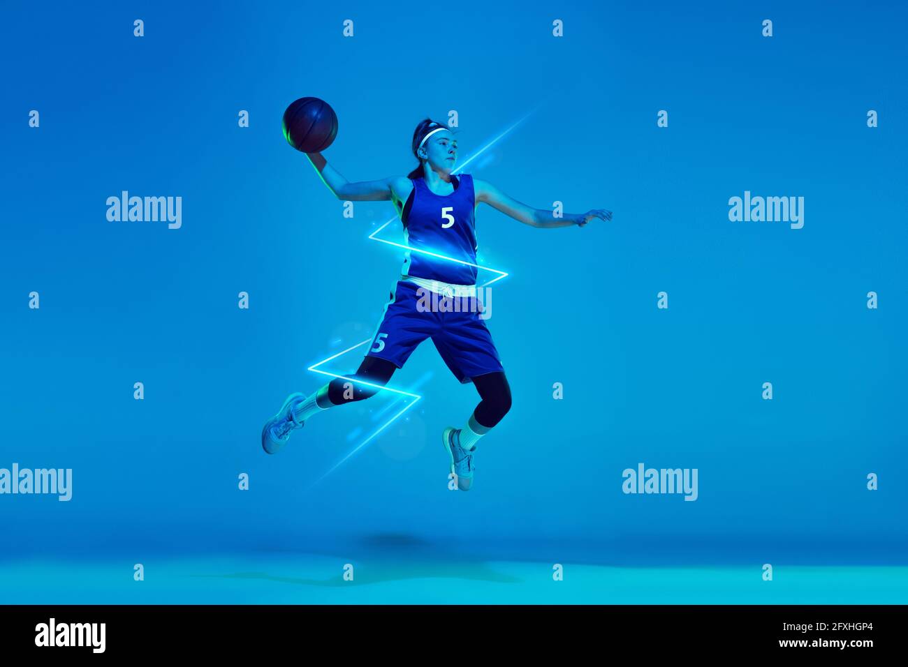 Young woman professional basketball player in jump isolated on blue ...