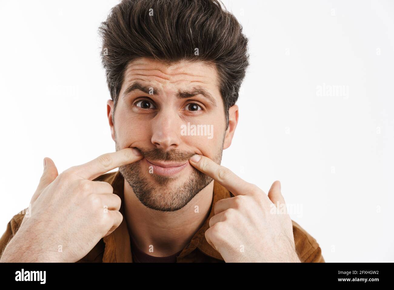 Confused young unshaven man pointing fingers at his cheeks isolated ...