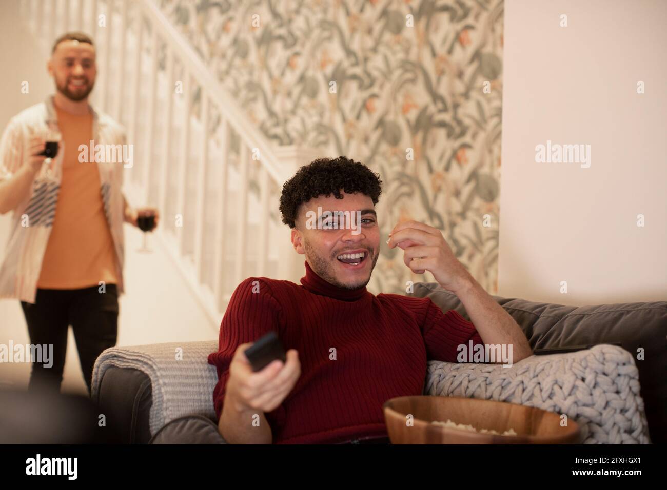 Happy young man with remote control watching TV on sofa Stock Photo - Alamy