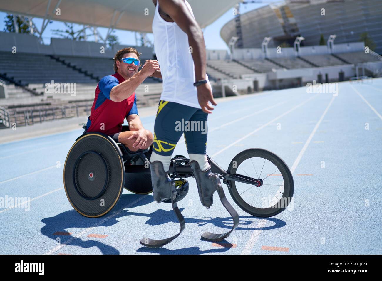 Male amputee and wheelchair athletes shaking hands on sports track ...