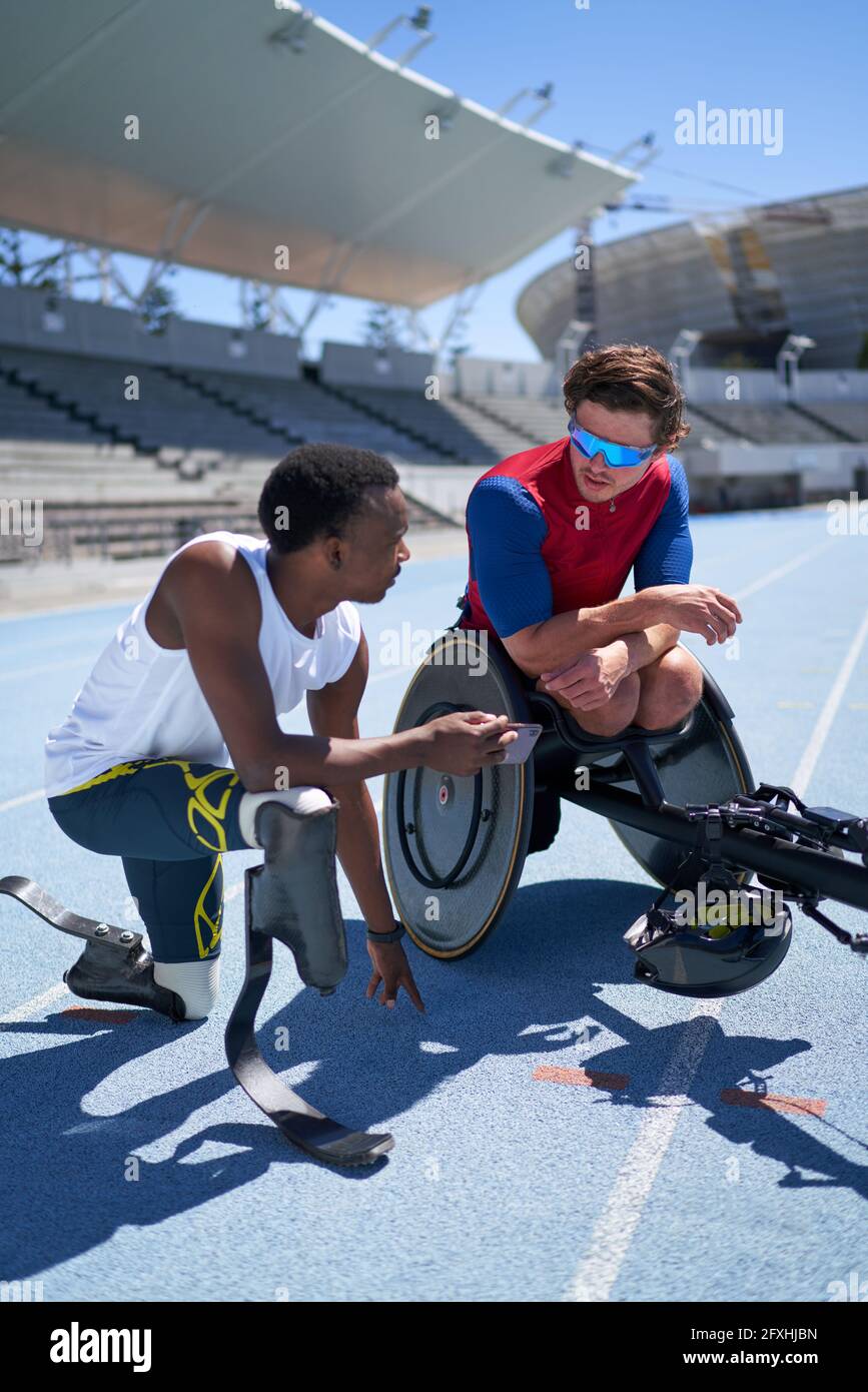Male amputee and wheelchair athletes talking on sunny sports track ...