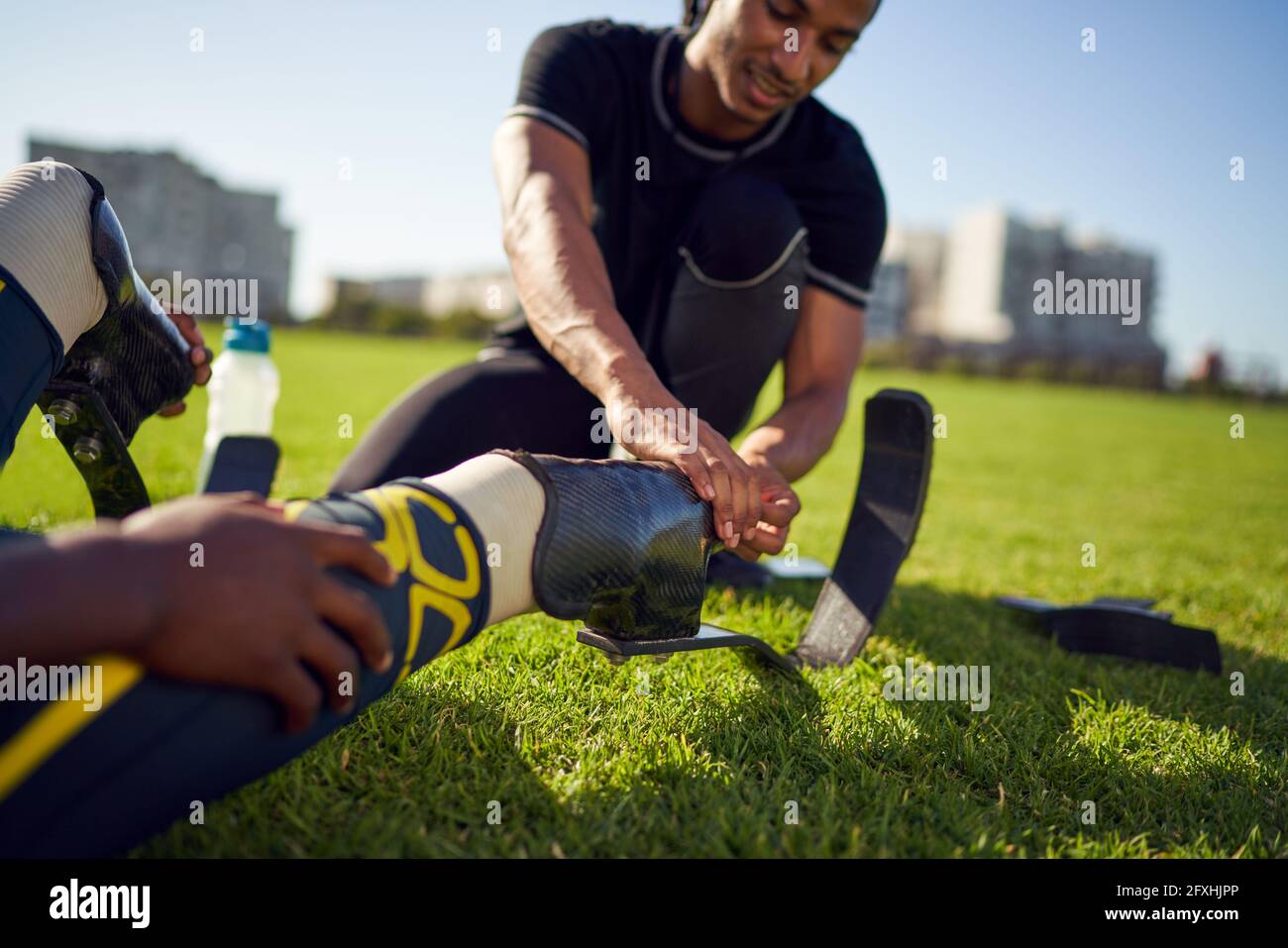 Coach helping amputee athlete with running blade prosthetic in park ...