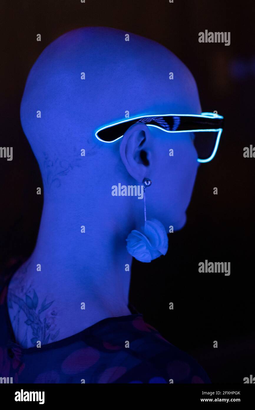 Stylish woman with shaved head wearing neon glasses in blue light Stock ...