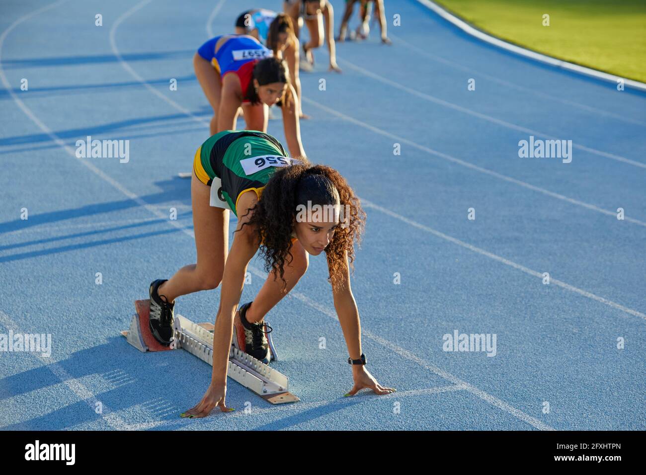 Female track and field athletes ready at starting blocks on blue track ...