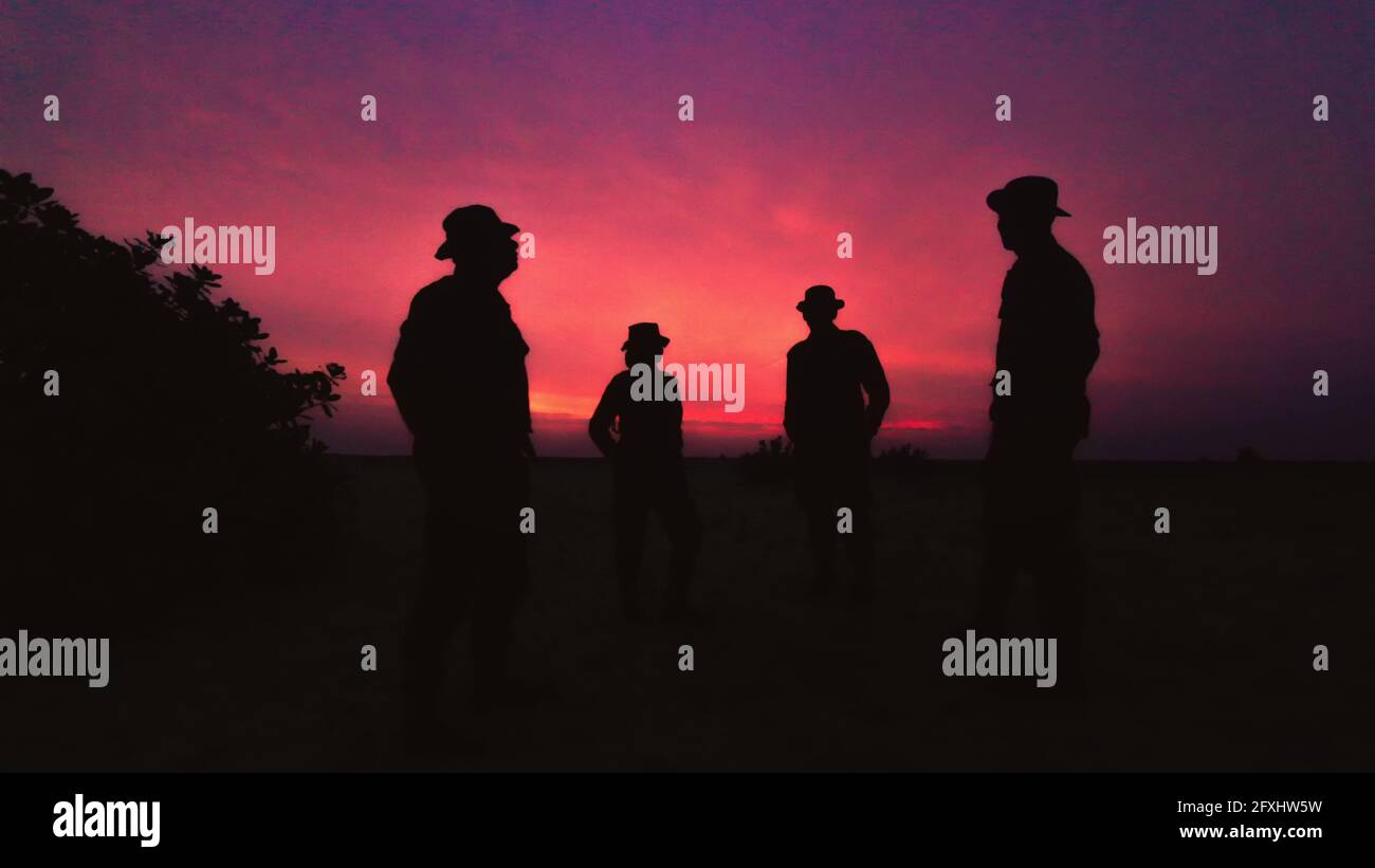 Silhouette of four men wearing hats standing against a beautiful sunset ...
