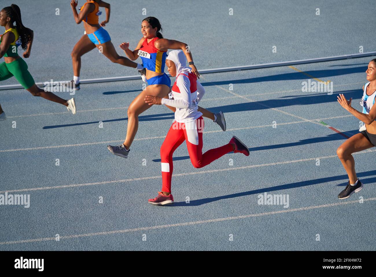 Female track and field athletes running in competition on sunny track ...