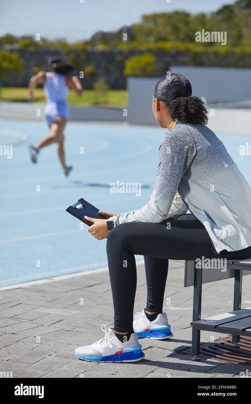 Female track and field coach watching runner on sunny track Stock Photo ...