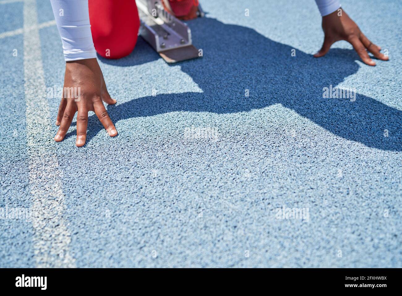 Close up hands of female track and field athlete at starting block ...