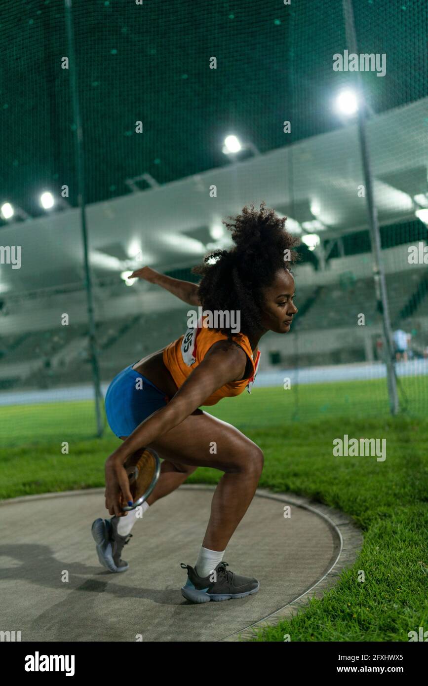 Female track and field athlete throwing discus in stadium at night ...