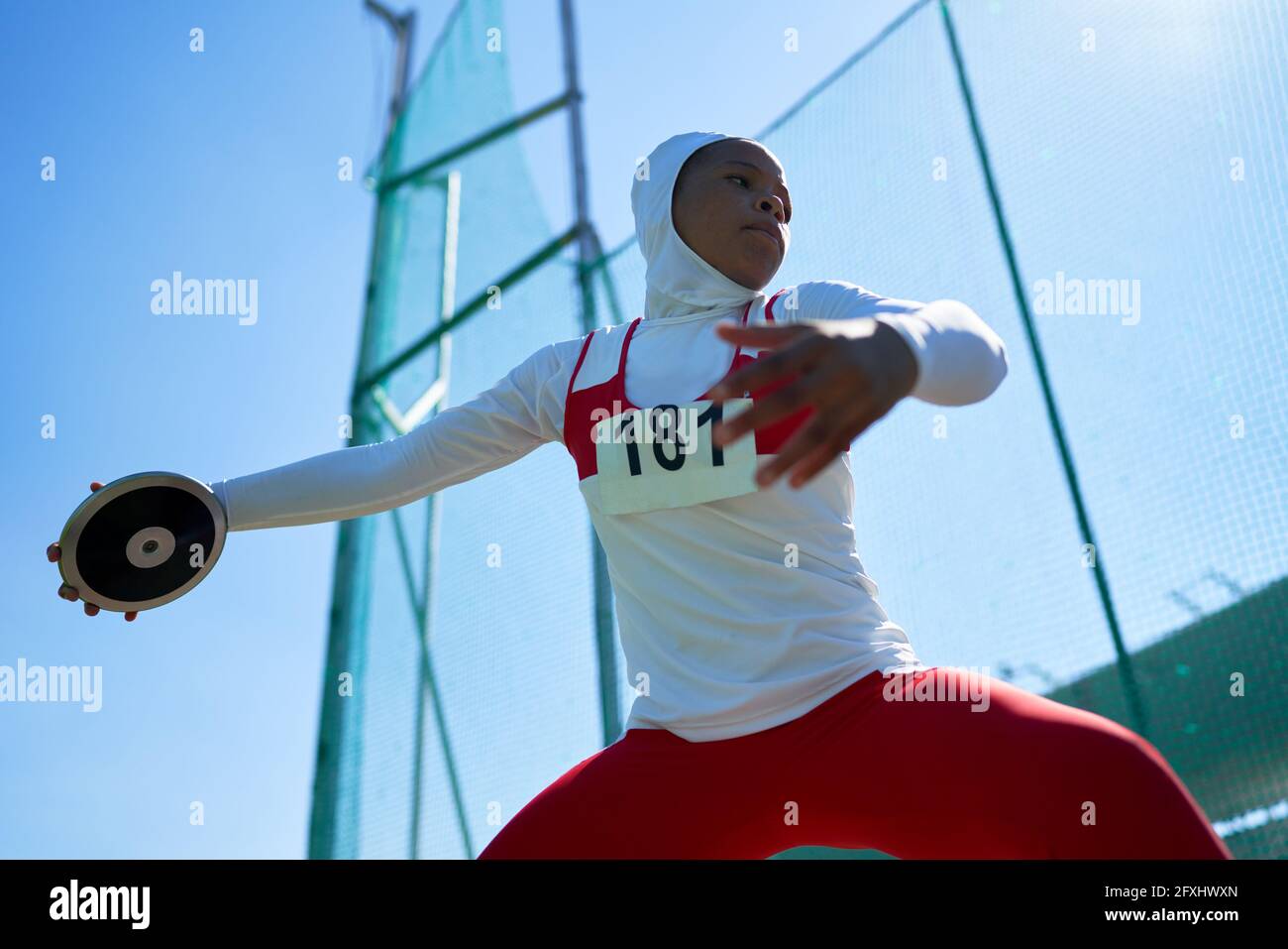 Determined female track and field athlete in hijab throwing discus ...