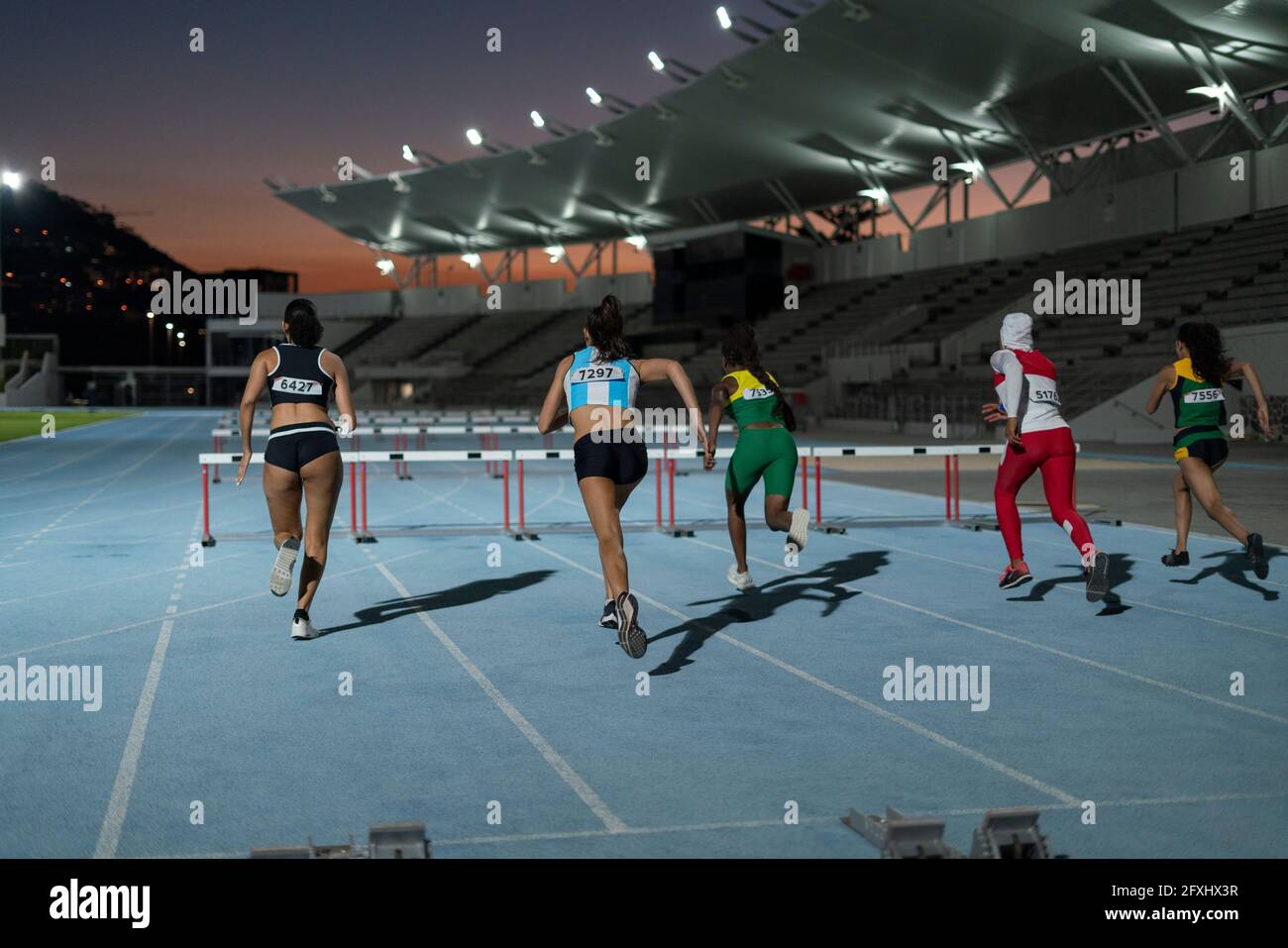 Female track and field athletes racing toward hurdles in stadium Stock ...