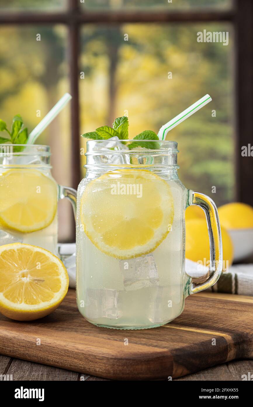 Glass of lemonade with lemon and mint by a window with rural background ...