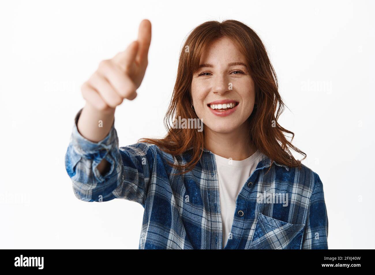 Young redhead woman laughing, pointing finger at tv screen and smiling ...