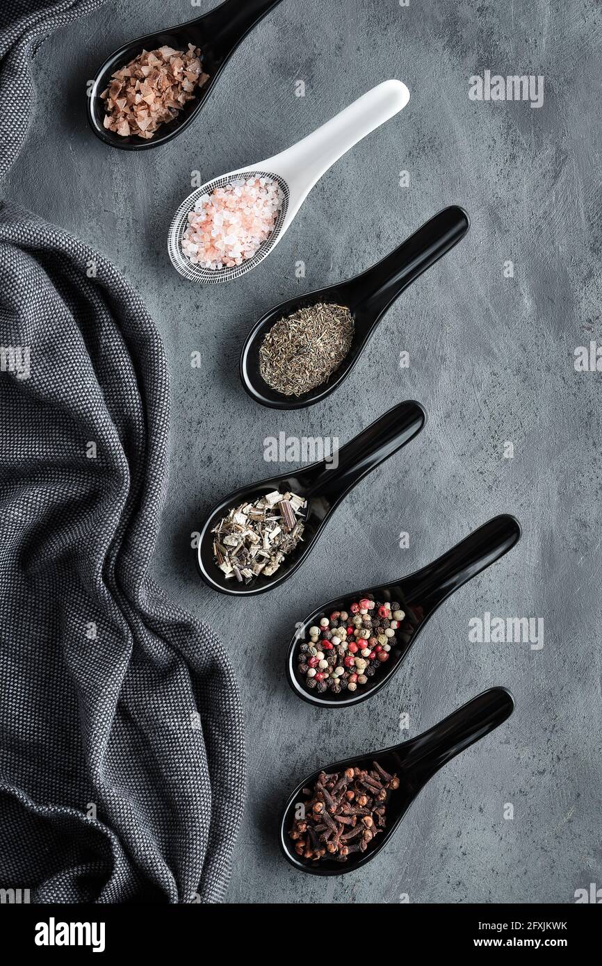 Various spices in ceramic oriental spoons and pinch bowls on dark grey ...