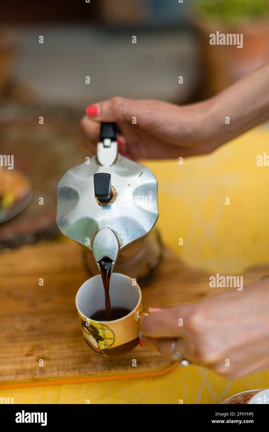 Woman's hand holding metal pot and pouring coffee into a white cup ...