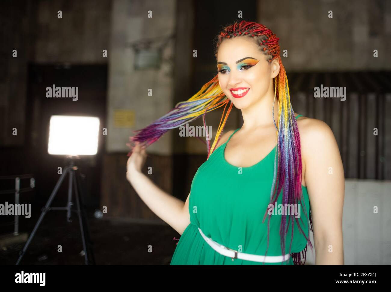 A girl with makeup and multi-colored African braids in a green dress ...