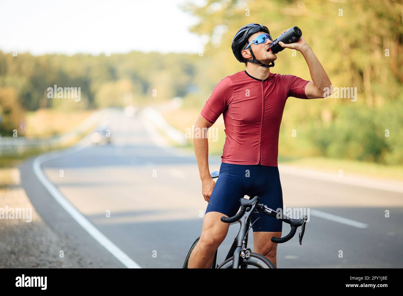 Muscular cyclist relaxing on bike and drinking water Stock Photo - Alamy