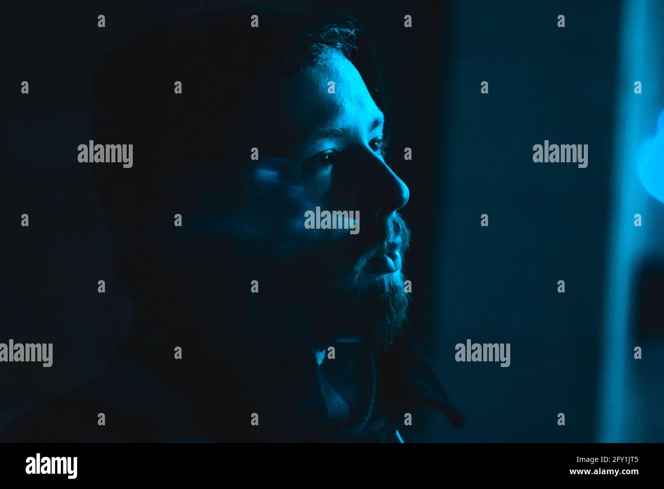 Portrait of smoking handsome man in a hood at the dark with cold blue ...