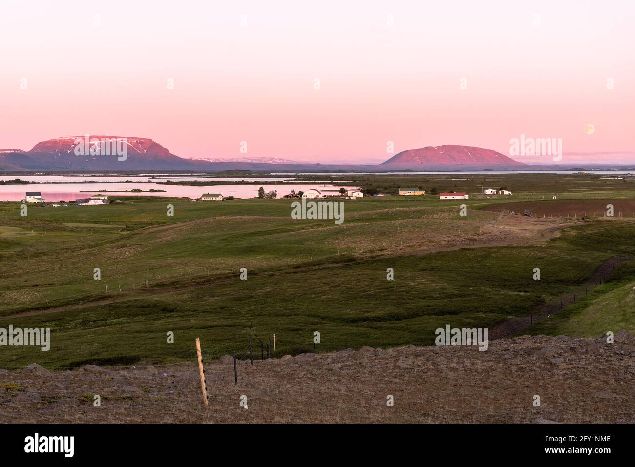 Farms along the shore of lake with mountains in background glowing pink ...