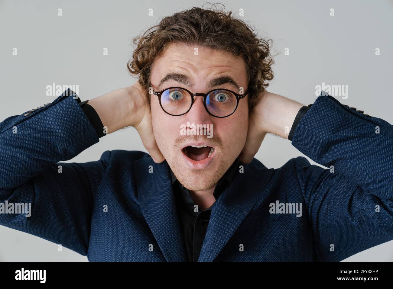 Shocked handsome man in eyeglasses screaming and covering his ears ...