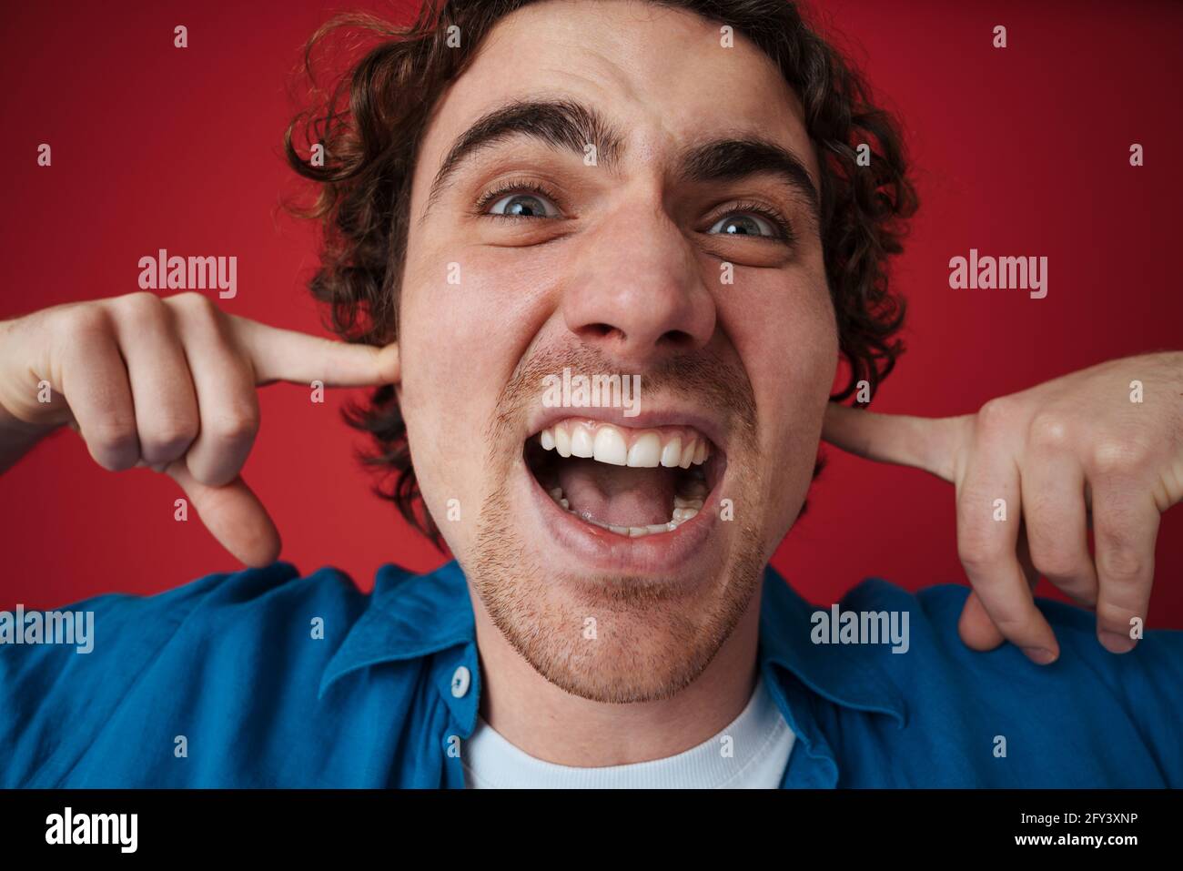 Stressed handsome man screaming while plugging his ears isolated over ...