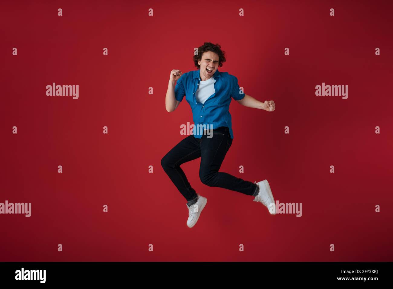 Excited handsome young man making fun while jumping isolated over red ...