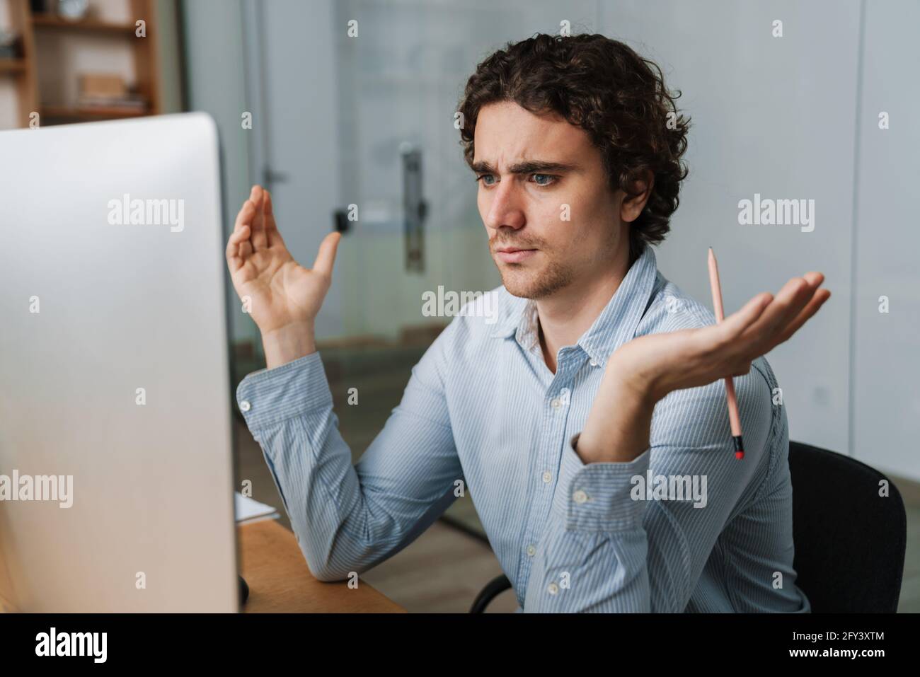 Displeased young businessman gesturing in confusion while working on ...