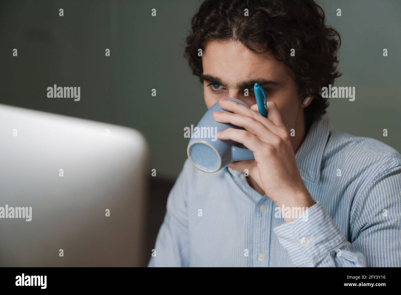 Caucasian young serious businessman drinking tea while working on ...