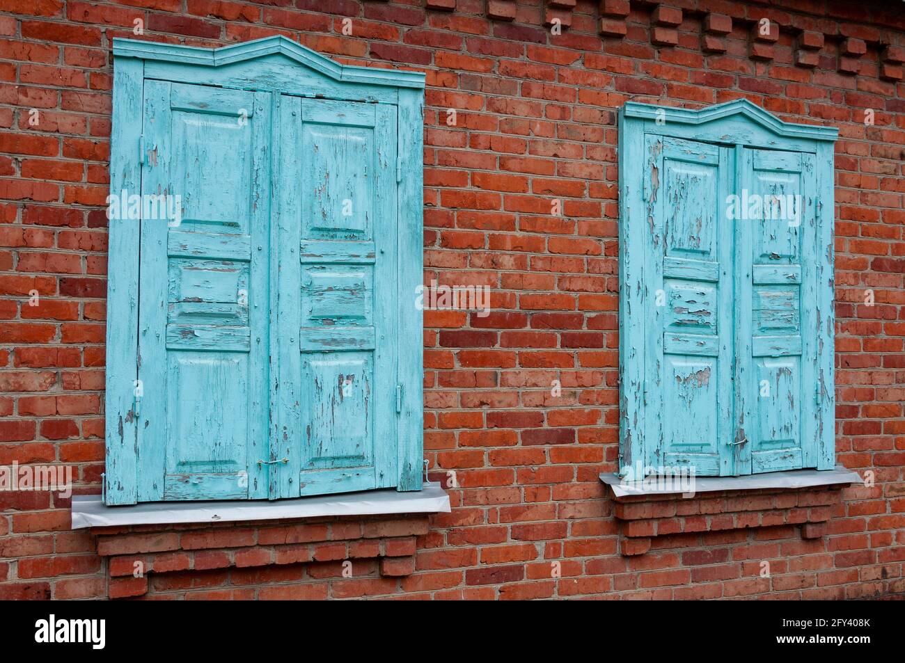 Two windows in old wall with closed blue shutters. Red brick wall ...