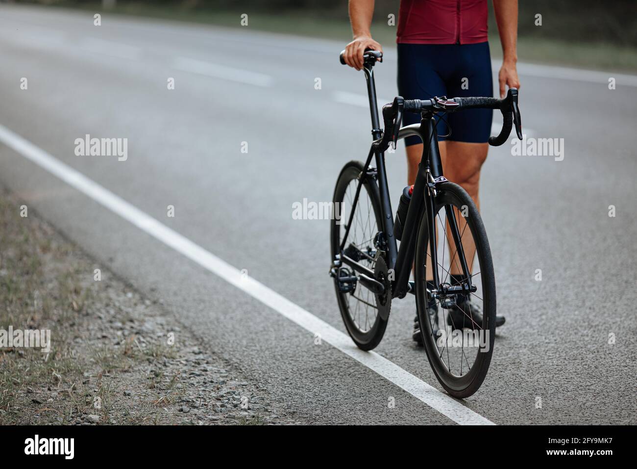 Male cyclist standing on road with black bike Stock Photo - Alamy