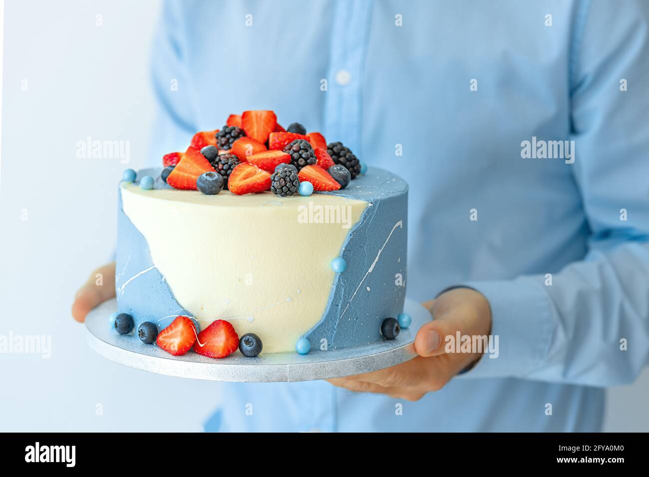 A man pastry shef holding a beautiful big cake with berries in his ...