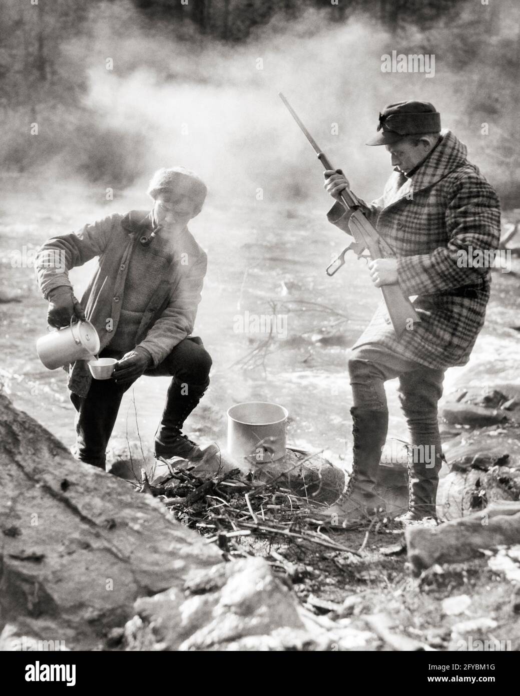 1920s TWO HUNTERS STANDING CAMPED BY STREAM ONE MAKING COFFEE OVER ...