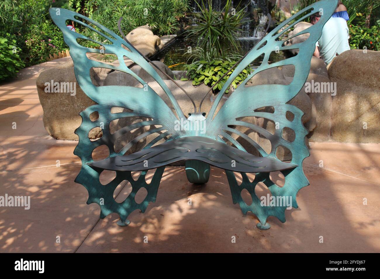 A large metal butterfly shaped bench in a park setting with plants, a ...
