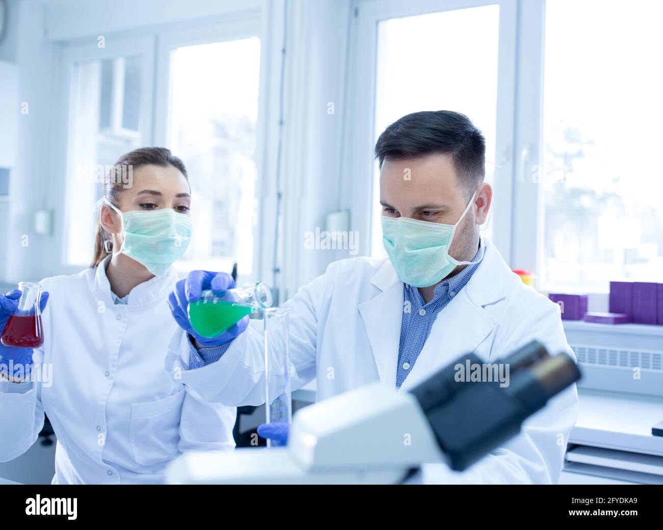 Young scientists researching experimenting holding erlenmeyer flask ...