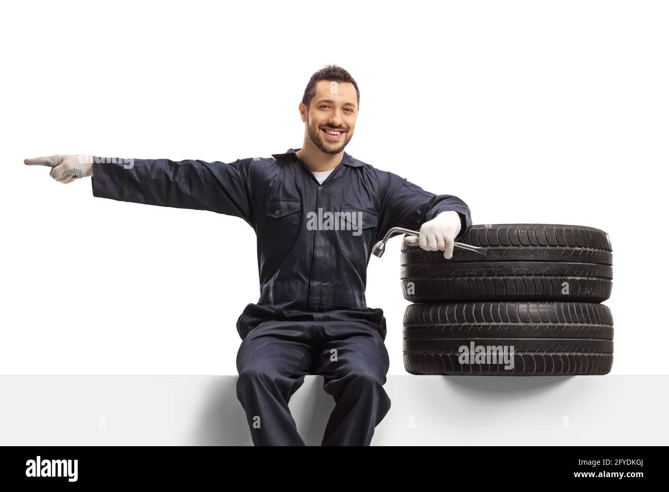 Auto mechanic worker sitting on a panel with tires and pointing to the ...