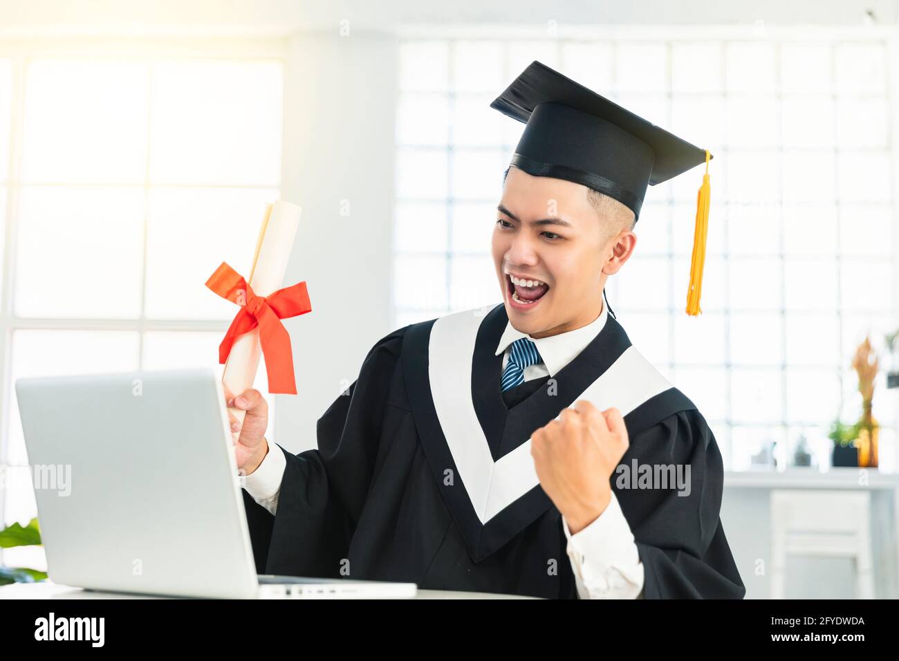 Happy male graduation watching the laptop and holding diploma and ...