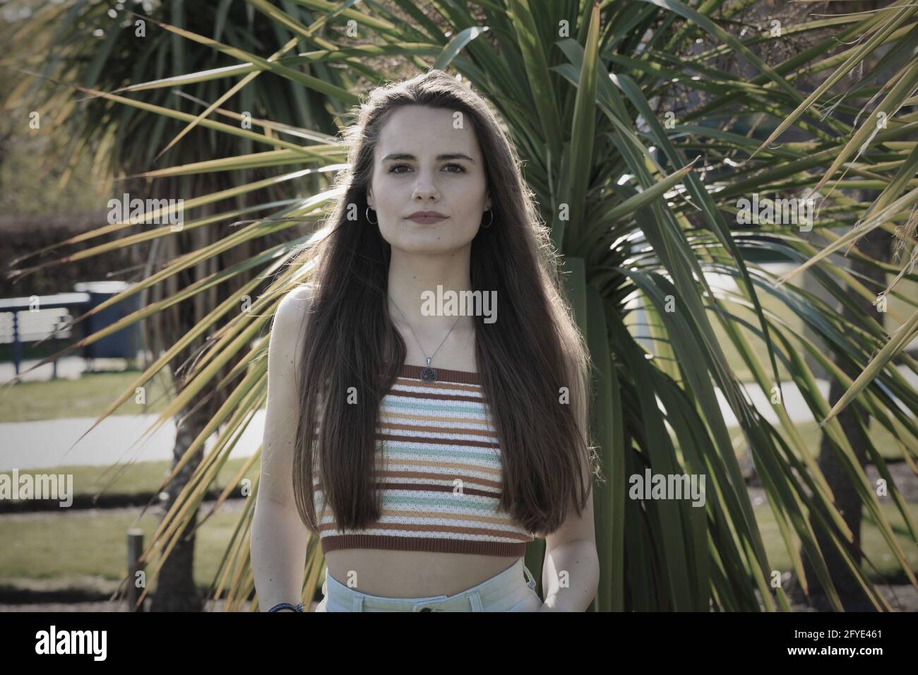 A portrait of a young brunette woman standing near a palm tree in a ...