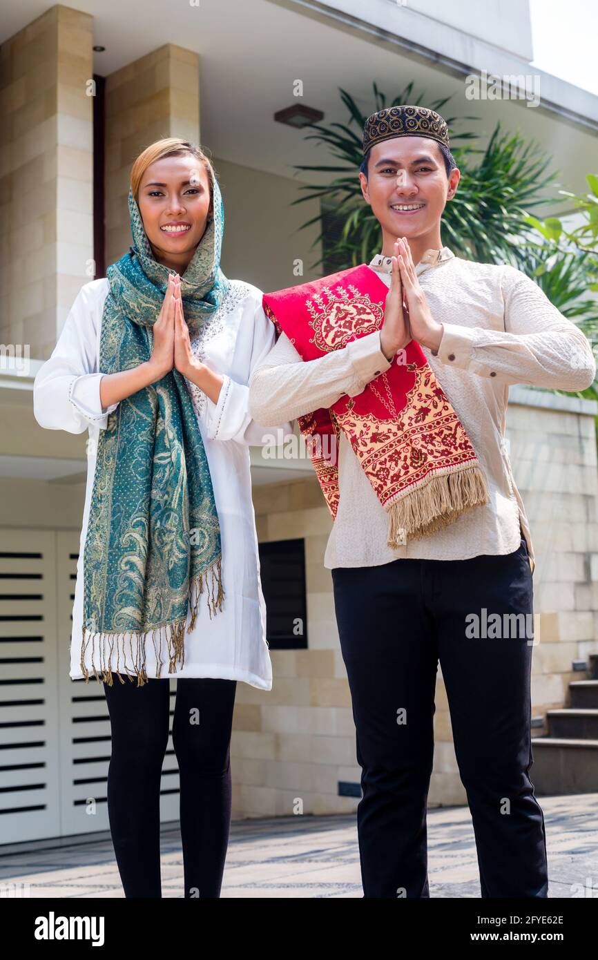 Asian Muslim man and woman welcoming guests wearing traditional dress ...