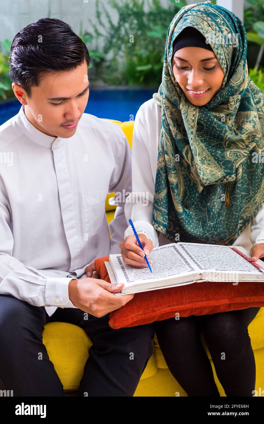Asian Muslim man teaching woman reading Koran or Quran in living room ...