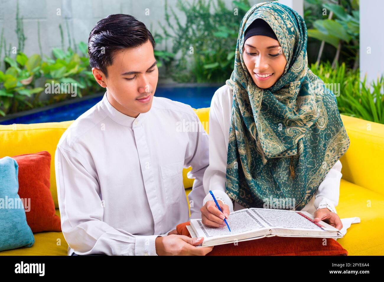 Asian Muslim man teaching woman reading Koran or Quran in living room ...